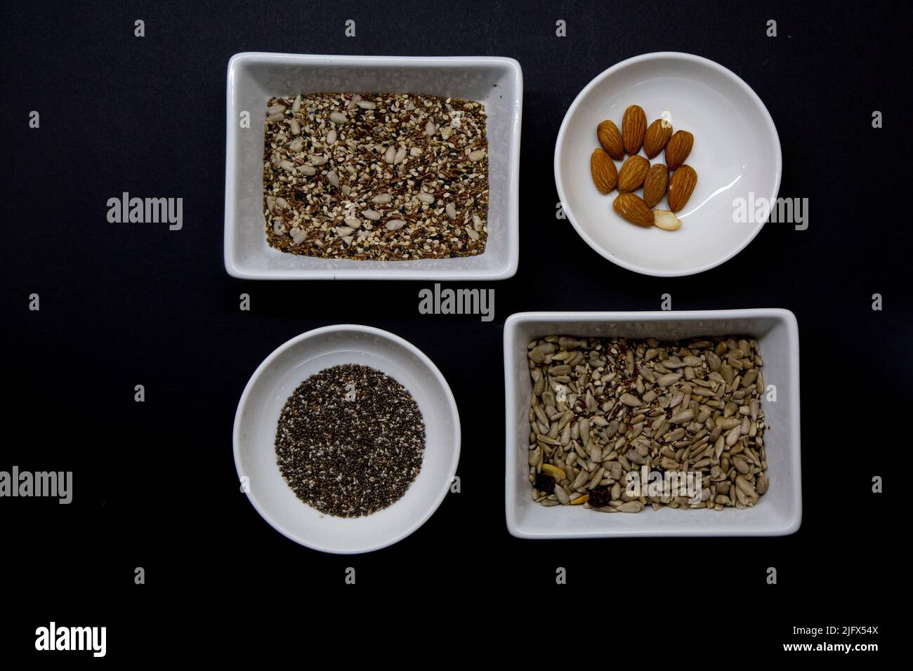 Dark background with white bowls contain healthy seeds for a vegan diet ...