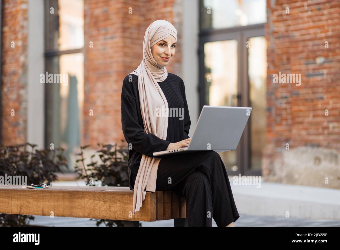 Pretty smiling muslim business woman in hijab sitting on bench and ...