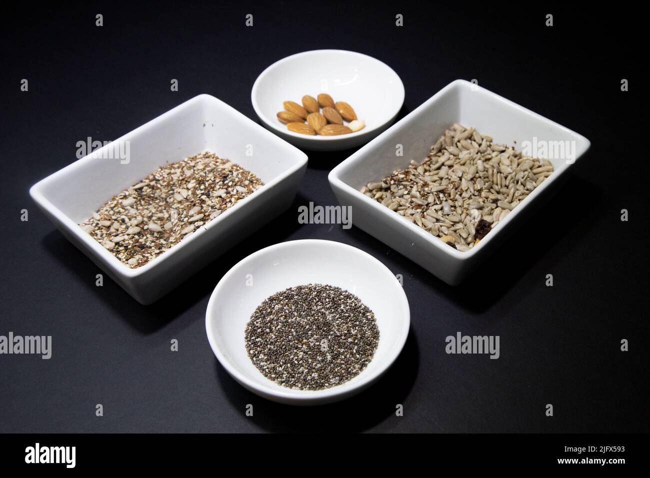Dark background with white bowls contain healthy seeds for a vegan diet ...