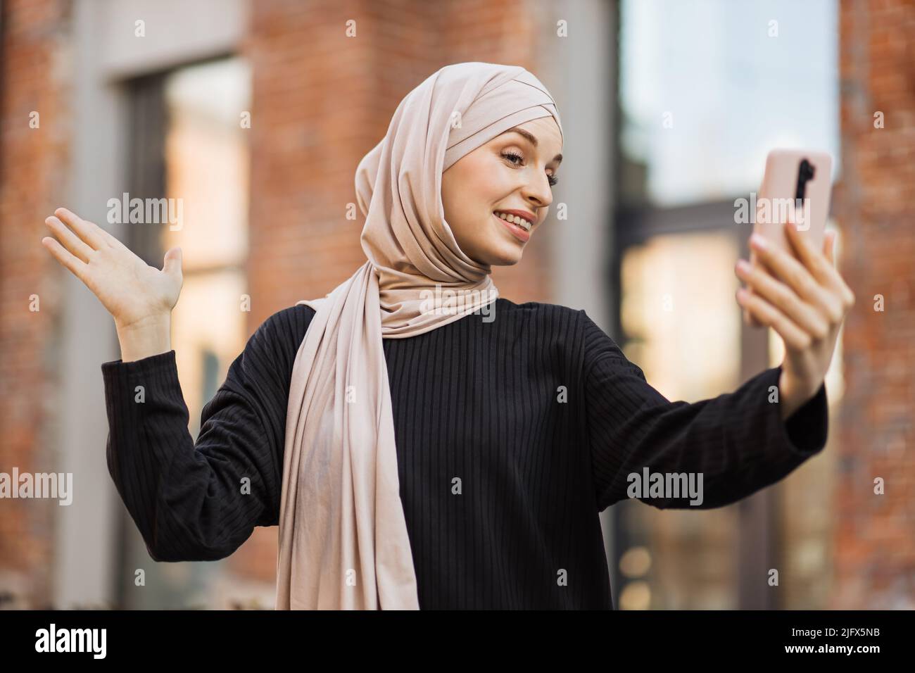 Young smiling happy muslim woman doing video call using smartphone at ...
