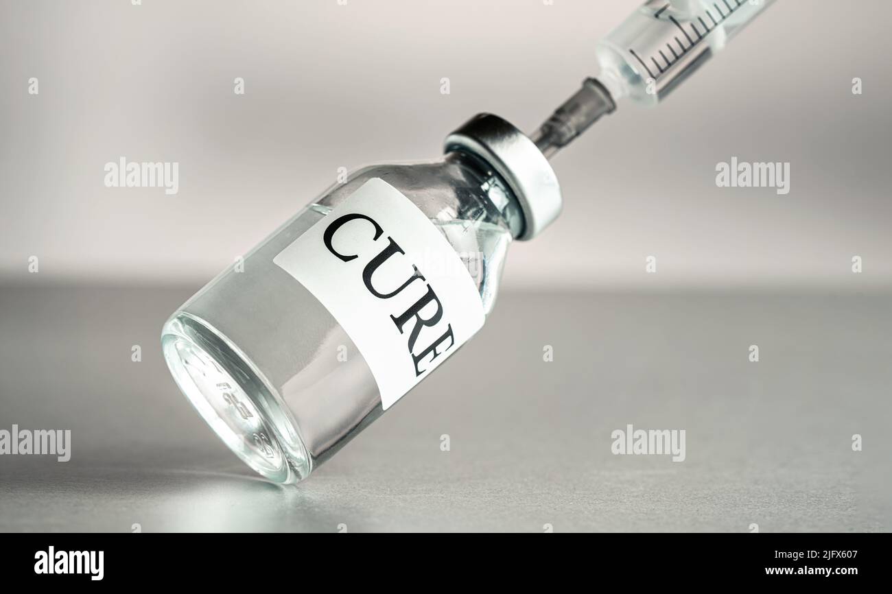 Glass vaccine vial with label Cure on white board, hypodermic syringe ...