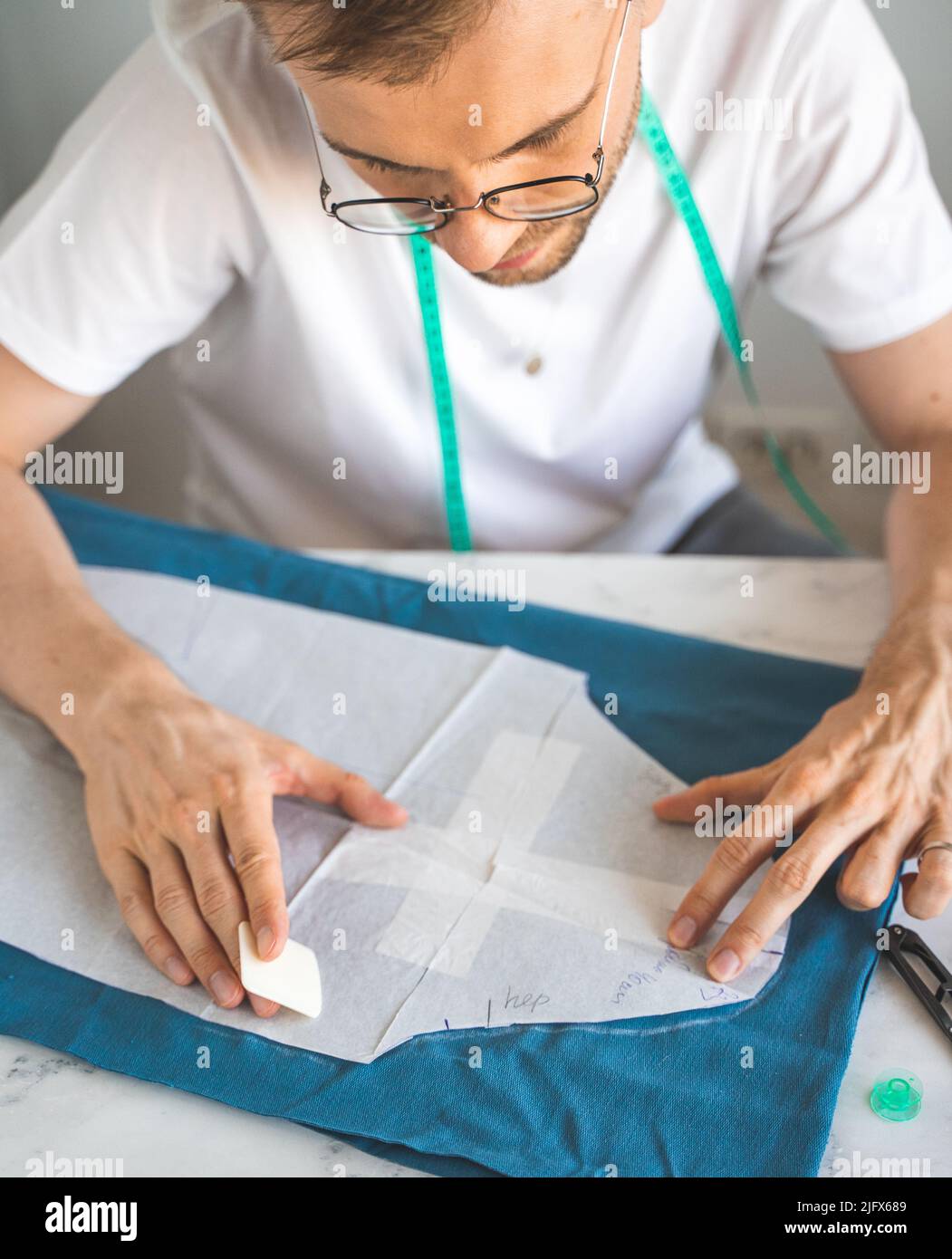A self-taught seamster in white t-shirt and glasses works with fabric ...