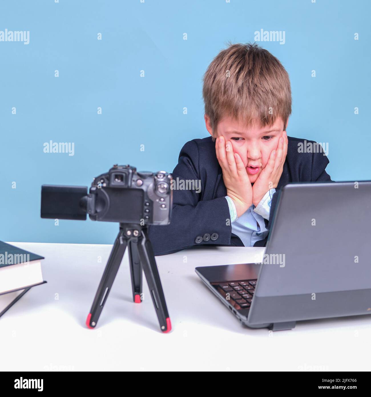 A boy in a school suit writes with a camera at a computer during ...