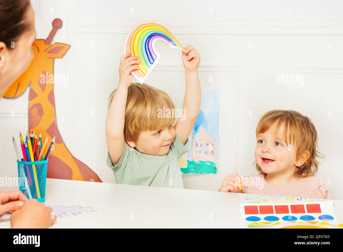 Little kids hold rainbow card at development class Stock Photo - Alamy