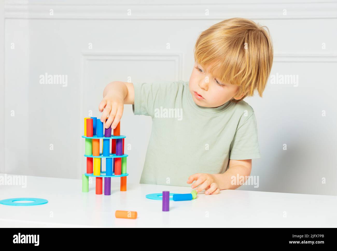 Concentrated boy constructs tower of color blocks on the table Stock ...