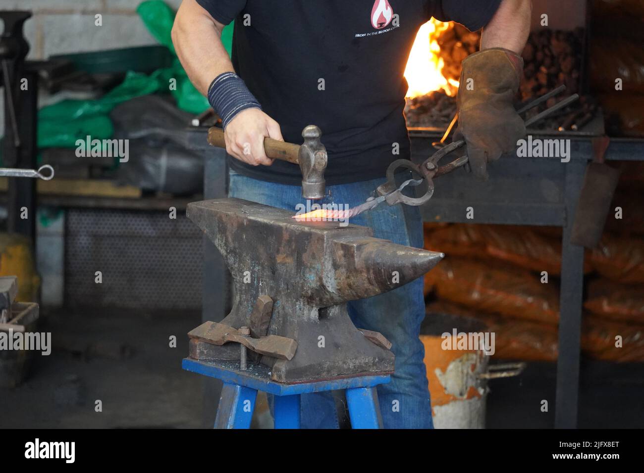 Close-up of the hands of a blacksmith using a hammer and anvil to shape ...