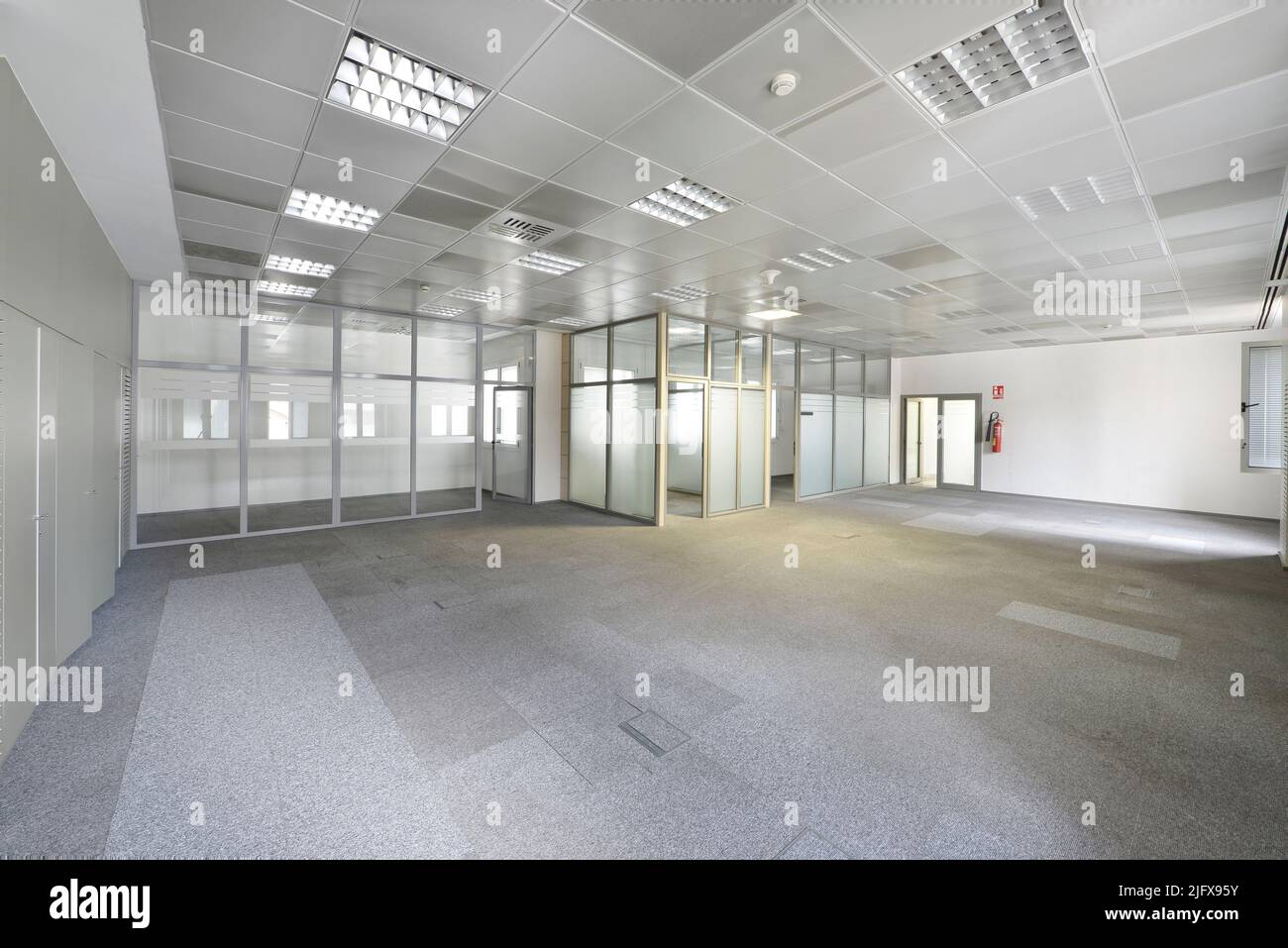 Large room to be dedicated to empty offices, with a gray carpeted floor ...