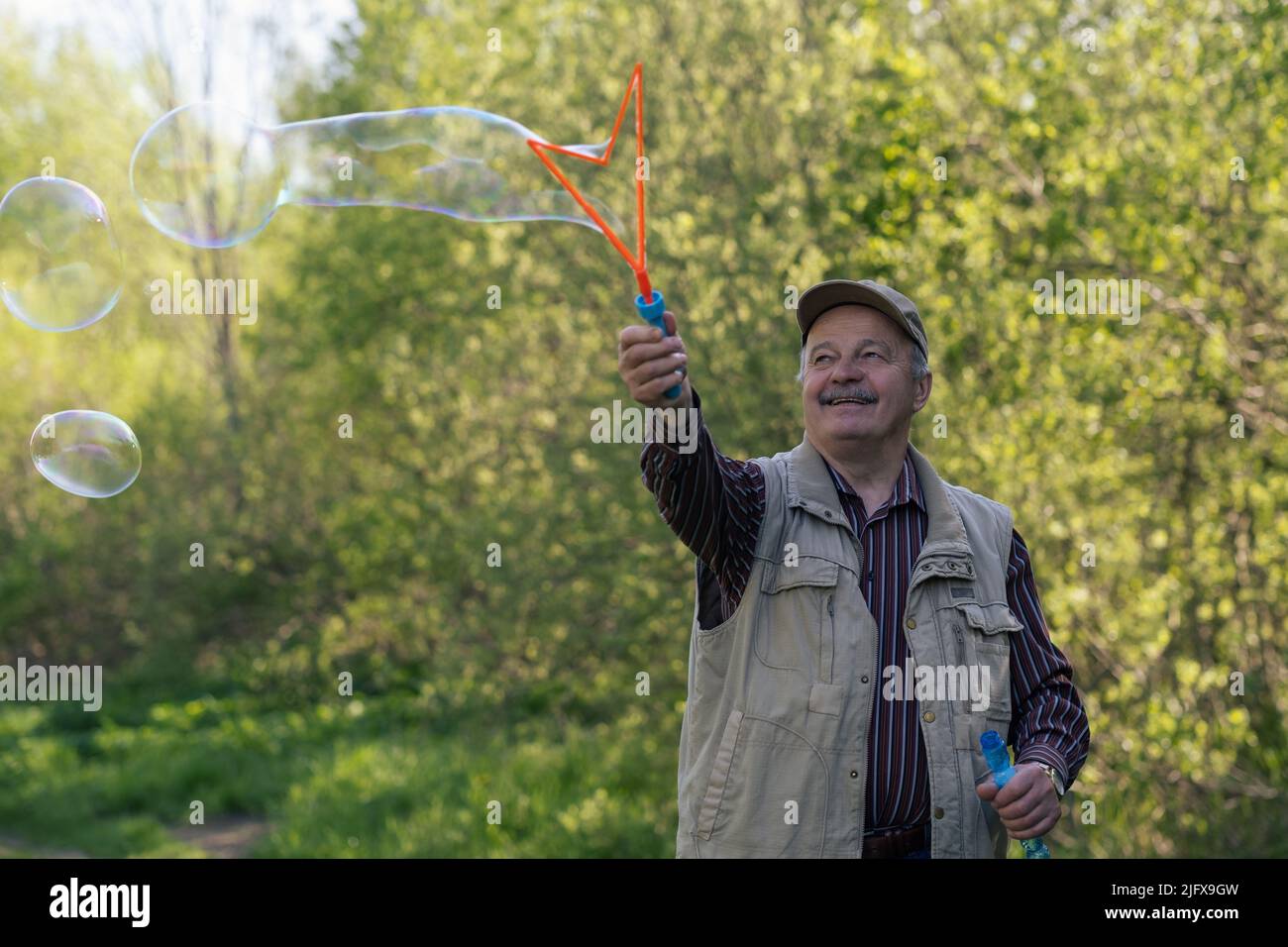 Senior active man plays with soap bubbles outdoor remembering childhood ...