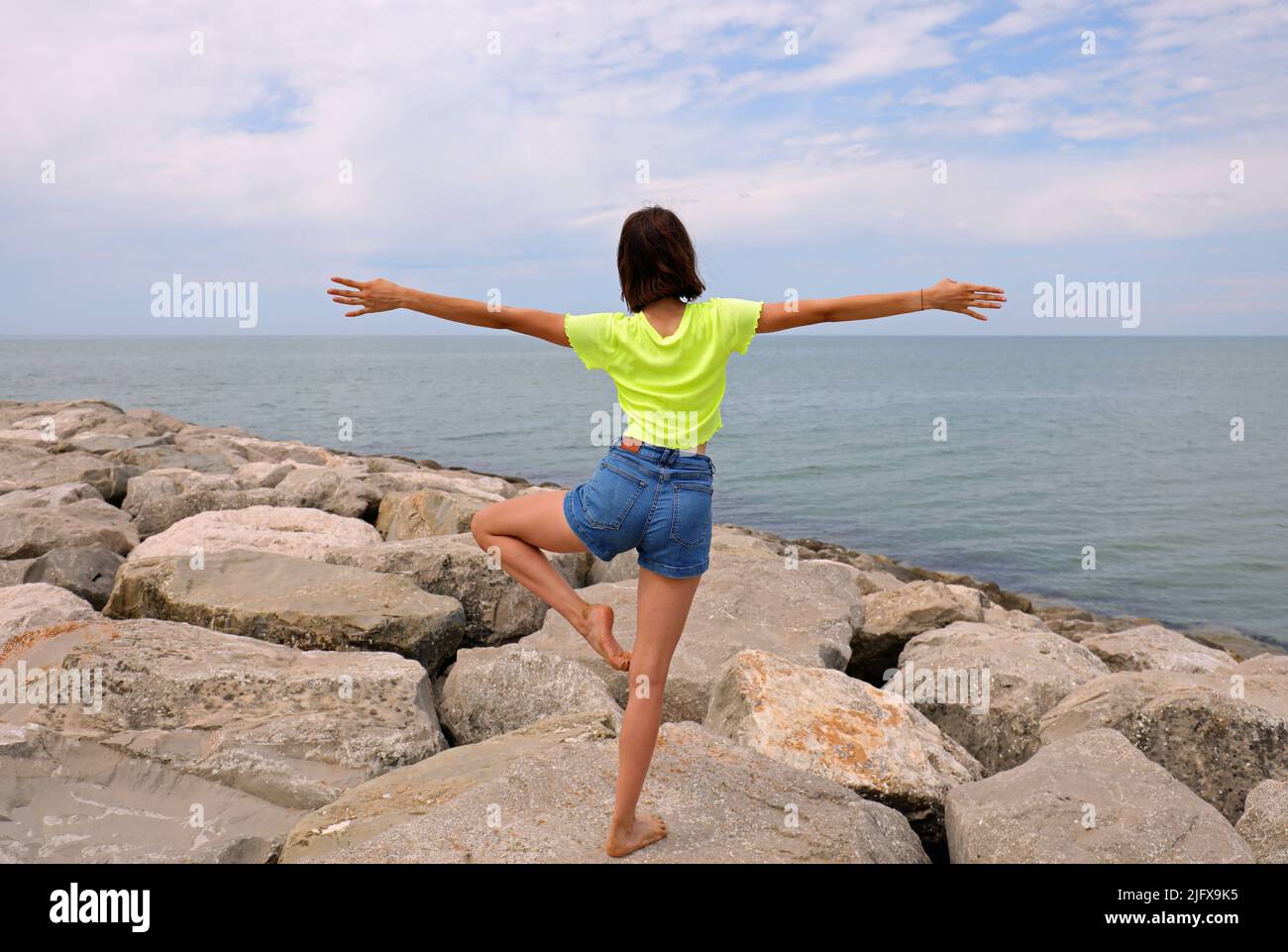 young slender girl on the rocks of the dike near the sea while ...