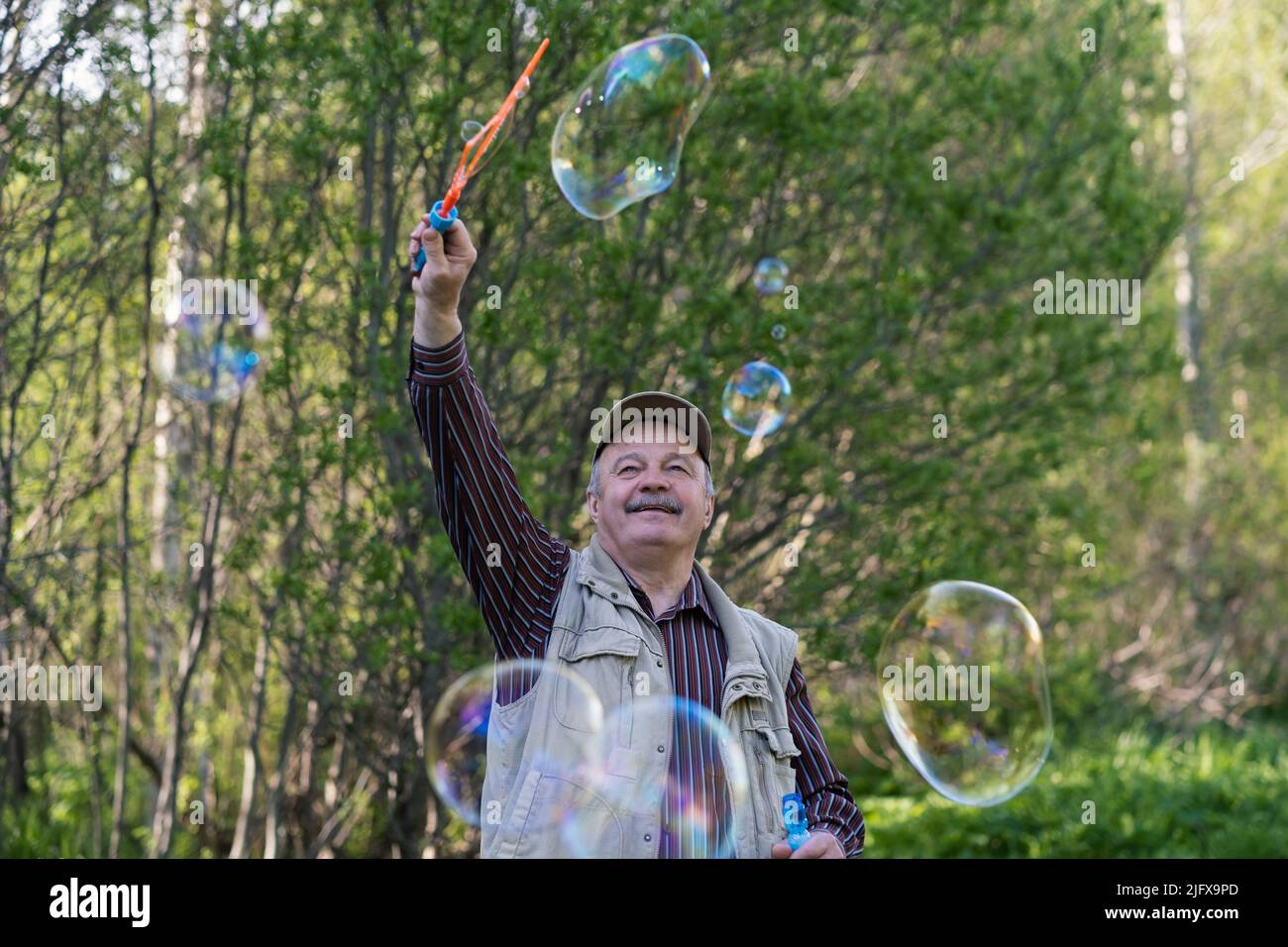 Senior active man plays with soap bubbles outdoor remembering childhood ...