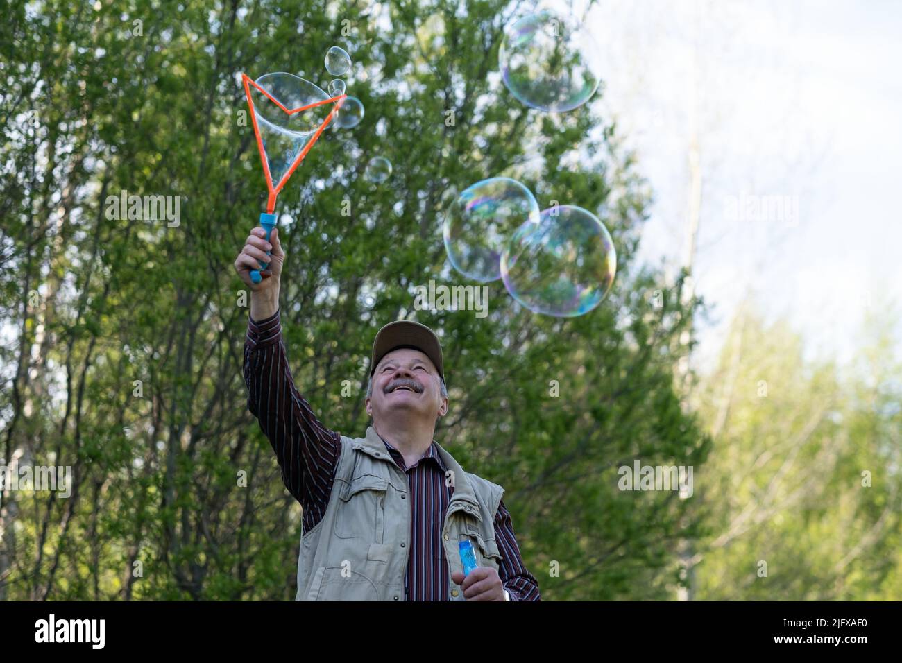 Senior active man plays with soap bubbles outdoor remembering childhood ...