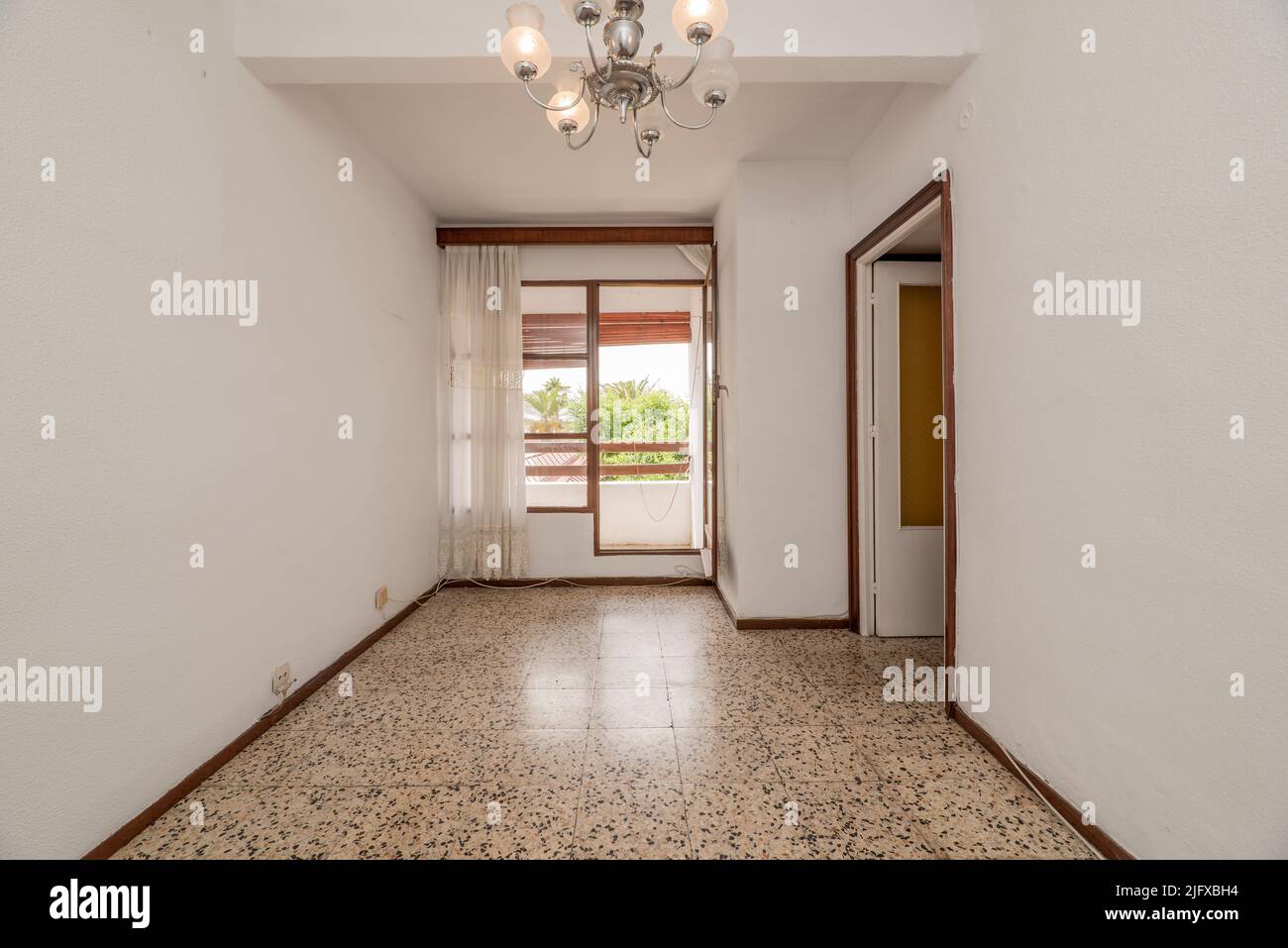 Empty room with old terrazzo floor, white walls and windows with access ...