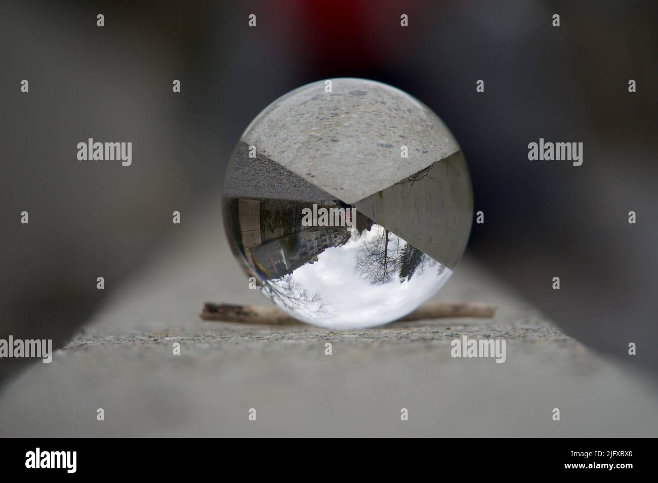 A closeup of a glass ball on a stone reflecting buildings and trees ...