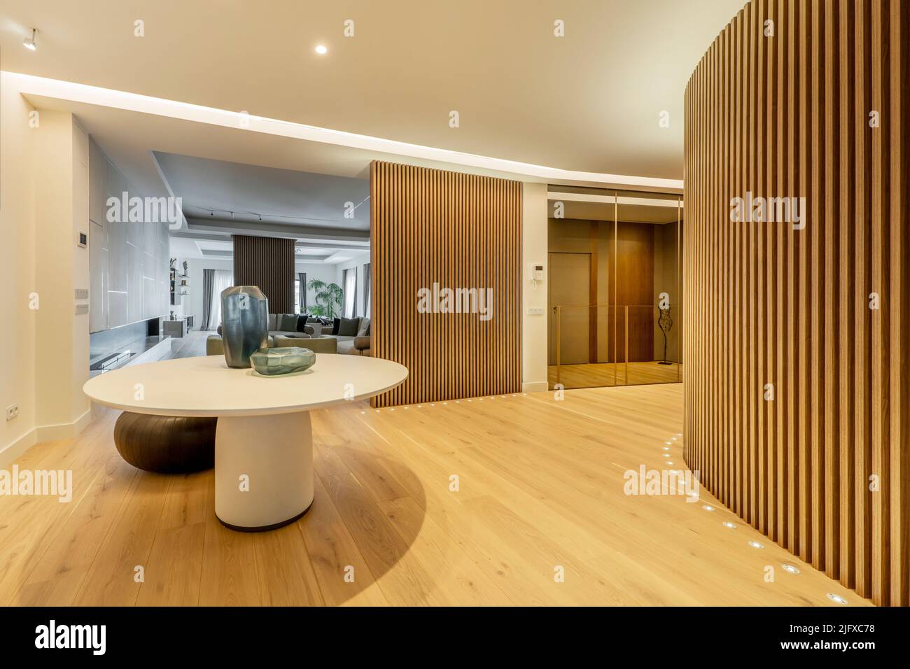 Hallway of luxury home with round table with vases, slatted walls and ...