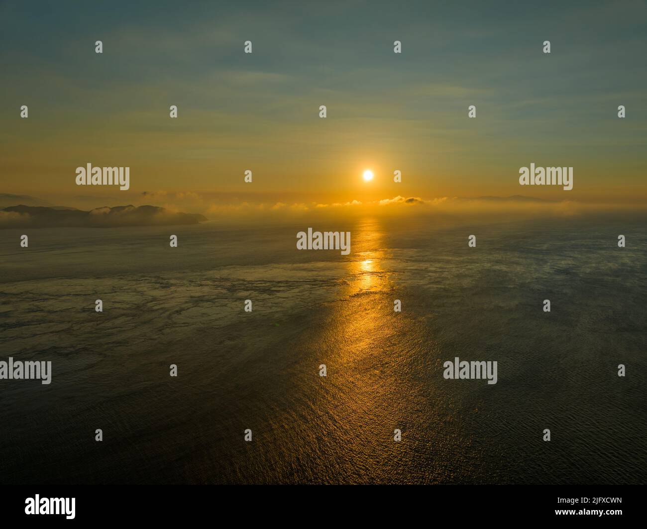 Low sun shines through clouds and reflects off open ocean at dawn Stock ...