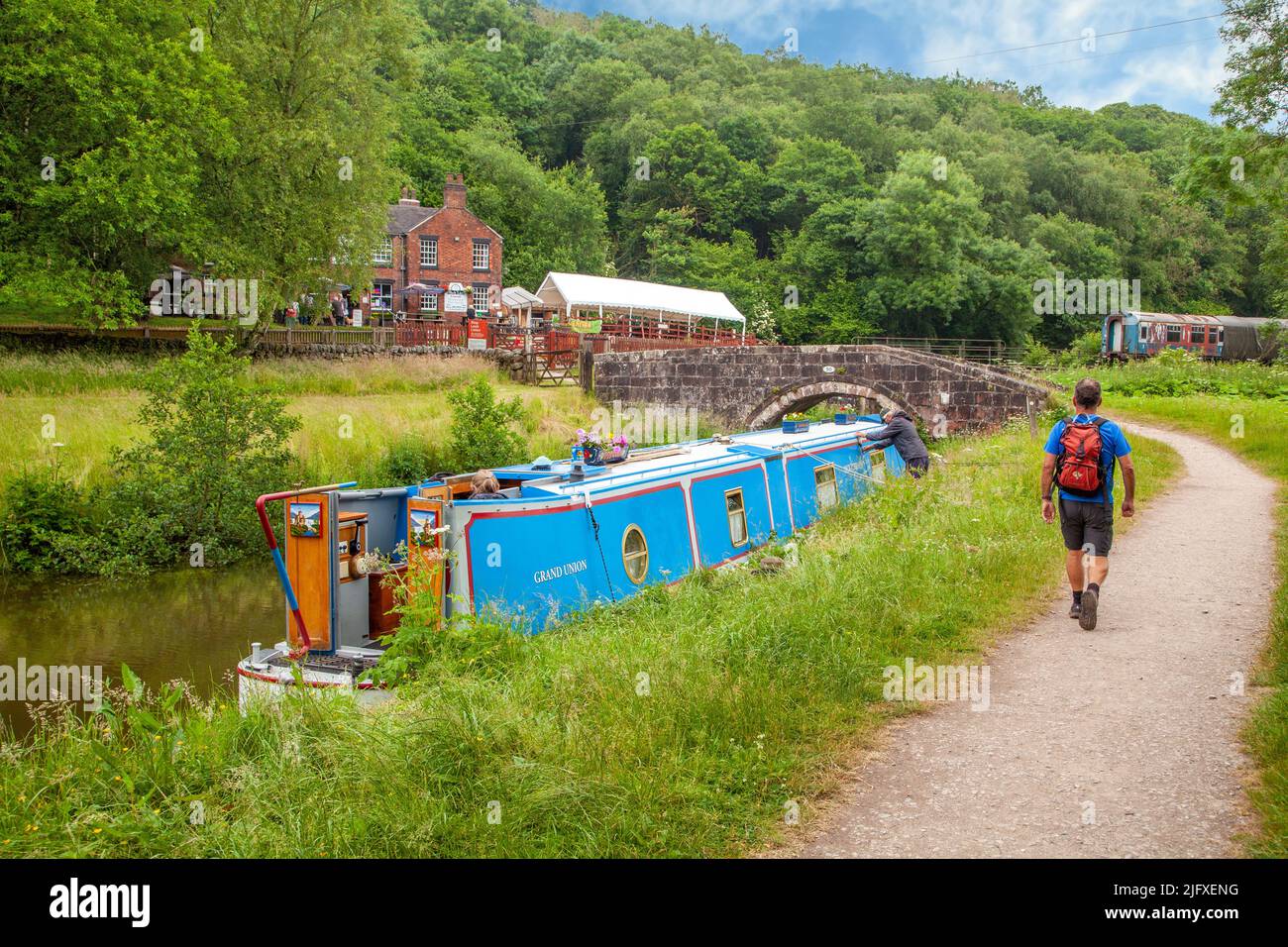 Man walking past canal narrowboat moored on the Caldon canal outside ...