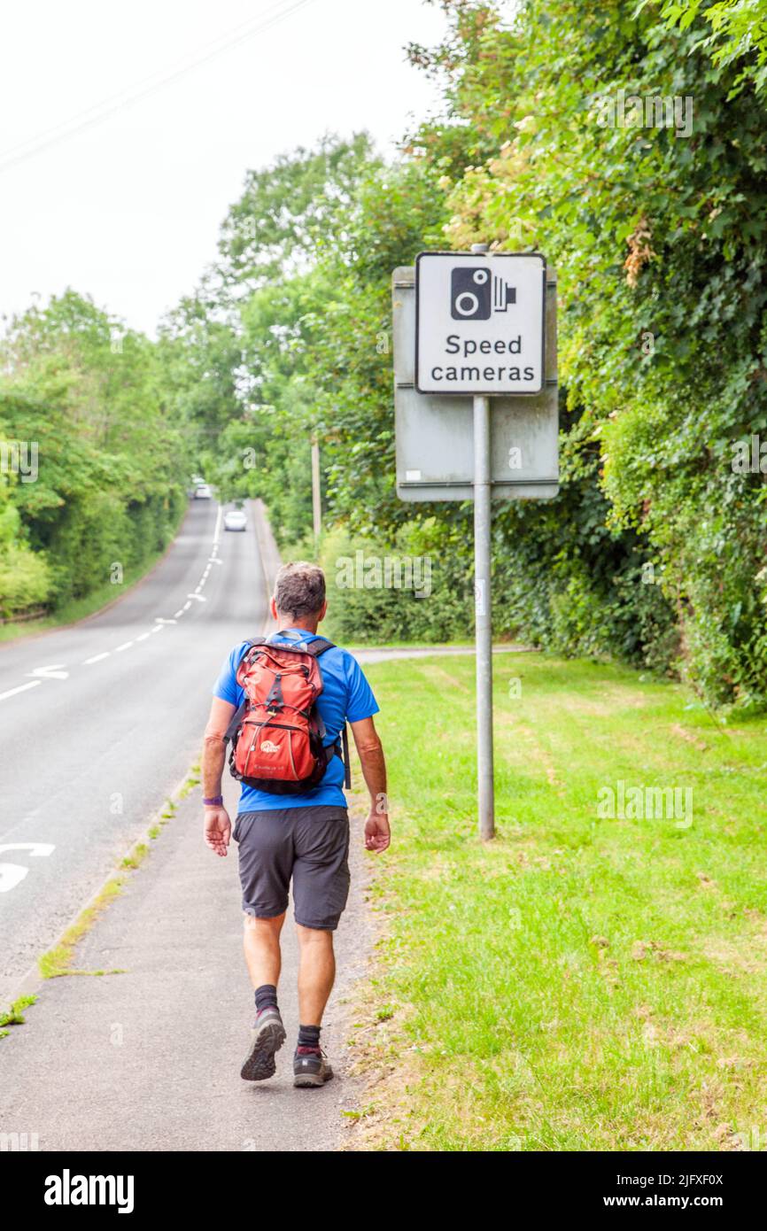 Man walking along a road pavement under a road sign saying speed ...