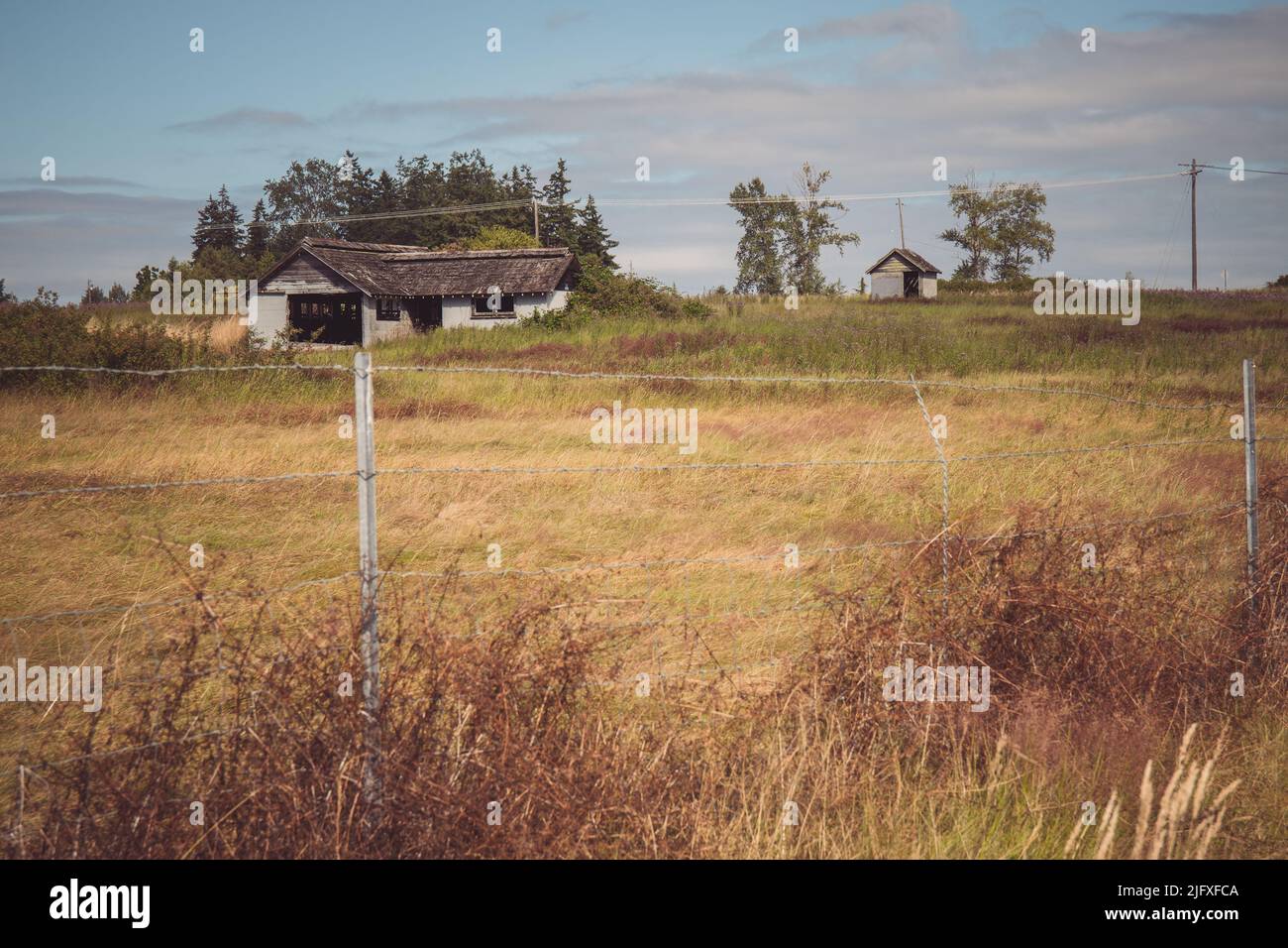 Old, Abandoned Buildings in Grass Field Behind Barbed Wire Fence Along ...