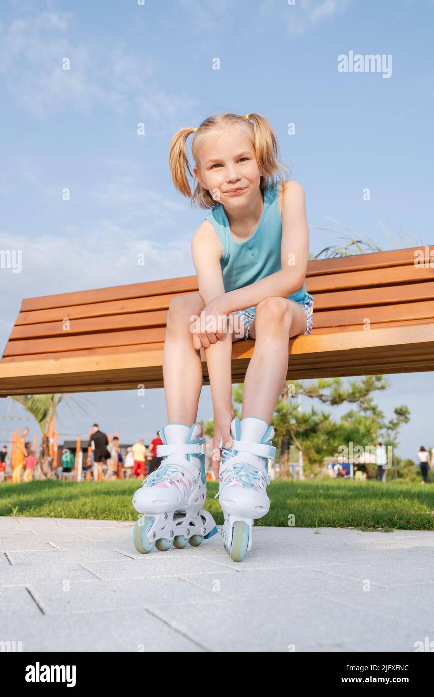 A Girl In Roller Skates Sits On A Park Bench And Fastens The Lock Stock