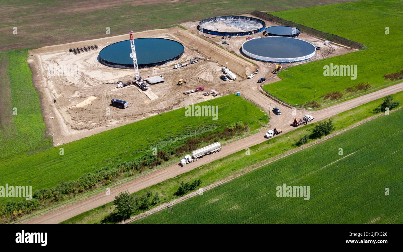 An oil well service rig and storage tanks are seen surrounded by farm ...
