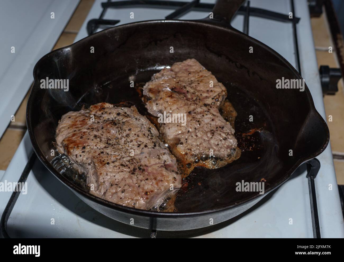 Two small beef loin steaks, seasoned with black pepper, frying in a ...