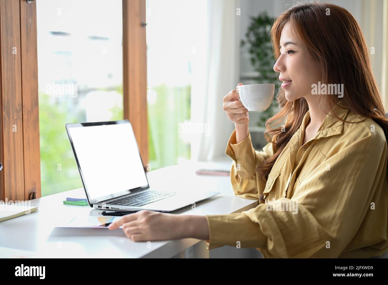 Beautiful Asian businesswoman or female manager relaxes siping a morning coffee while working at ...