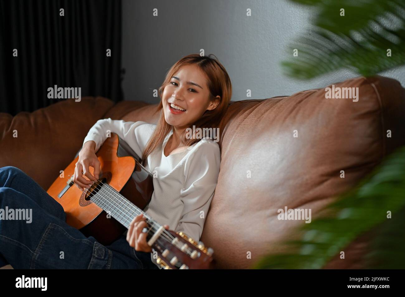 Attractive and talented millennial Asian girl sitting on comfy sofa in ...
