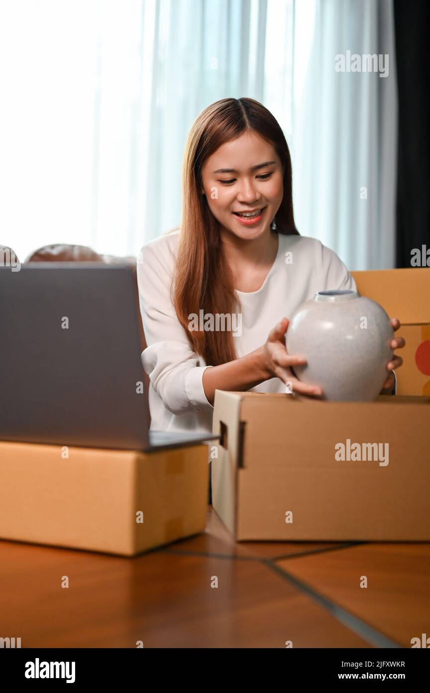 Charming millennial Asian woman online shop owner packing her goods ...