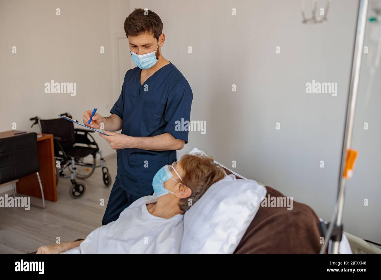 Doctor in mask writing down patient symptoms in hospital ward during ...
