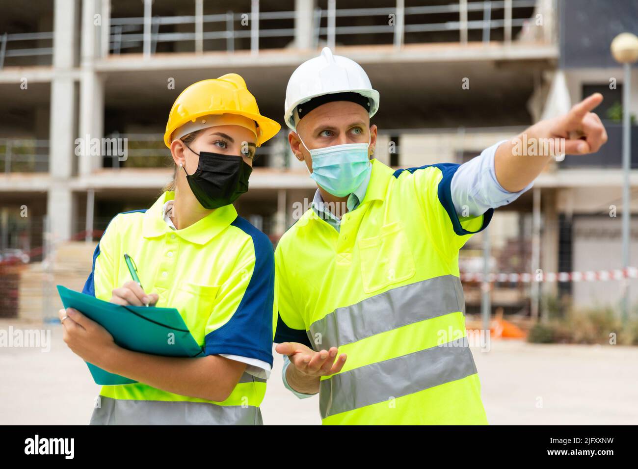 Male and female builders in masks talking in construction site Stock ...
