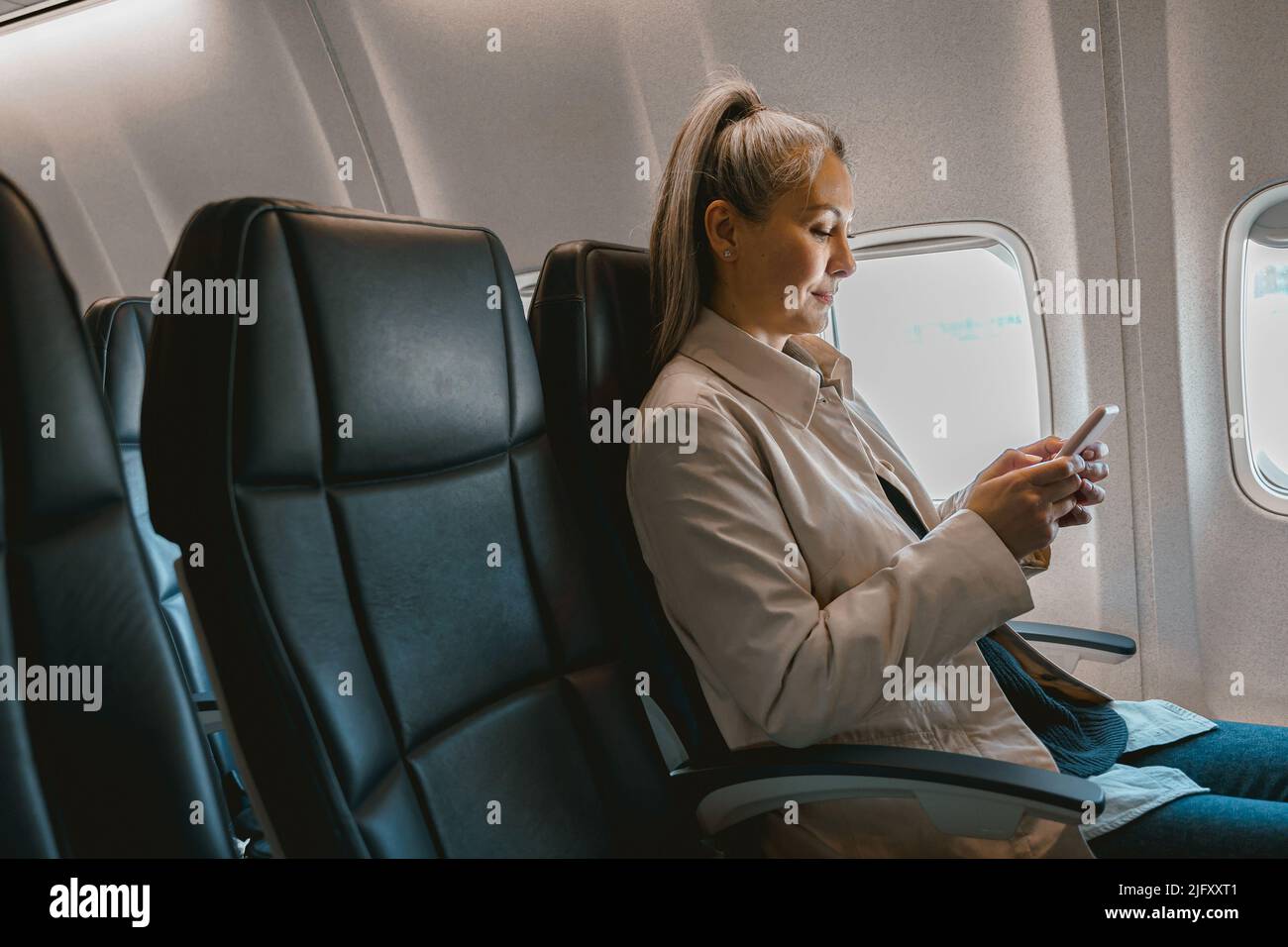 Beautiful Asian woman passenger sitting in the airplane and use phone during boarding Stock ...