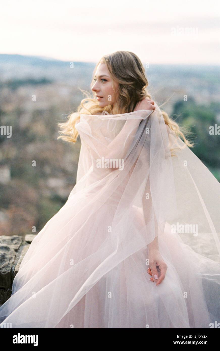 Bride in a dress with a cape sits on a stone wall. Bergamo, Italy Stock ...