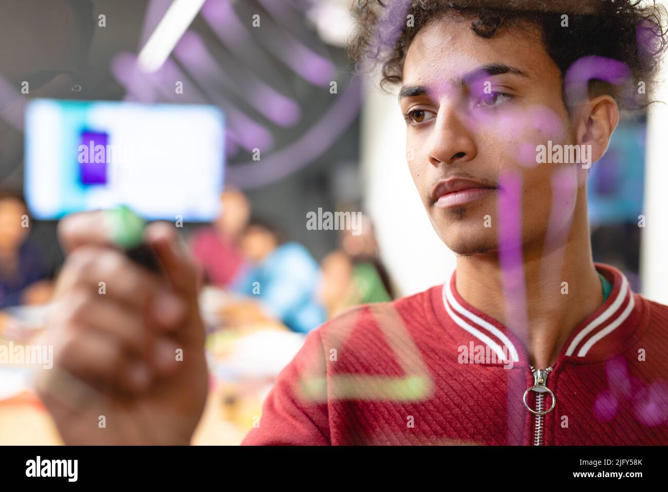 Young biracial male app developer drawing chart on glass in meeting ...