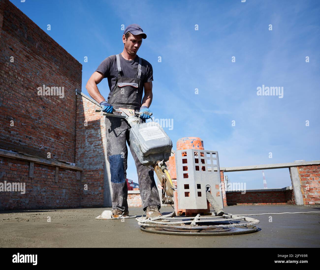 Full length of man laborer using troweling machine while screeding ...