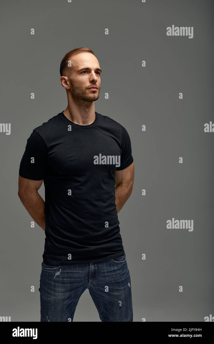 An attractive white man in jeans and black shirts tands in full growth ...