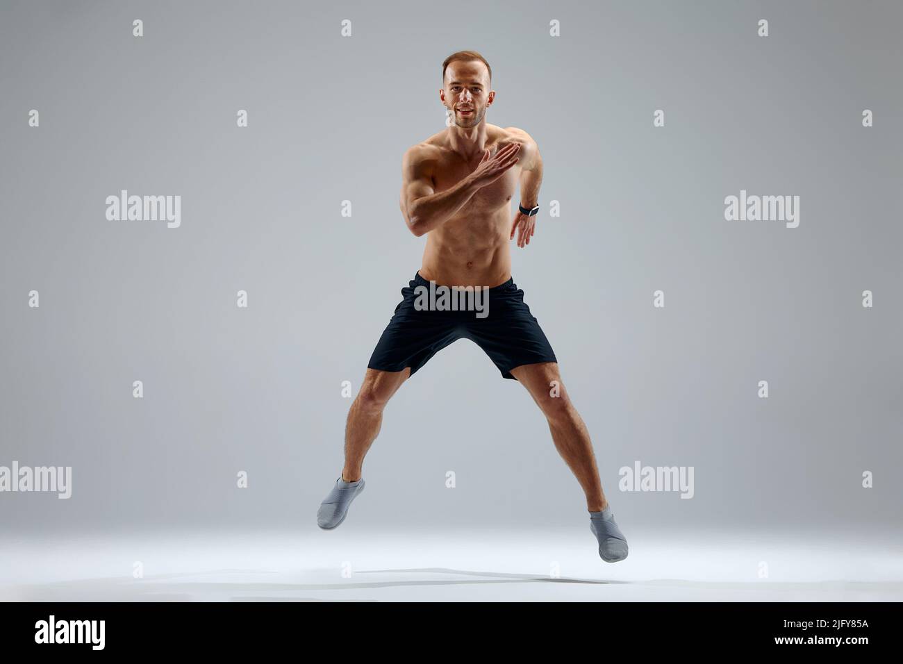 Developing endurance. Male athlete in motion isolated over gray studio ...