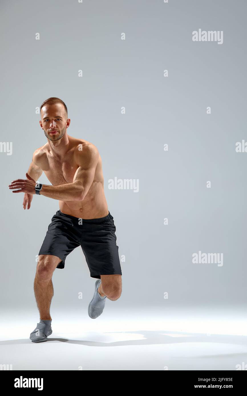 Developing endurance. Male athlete in motion isolated over gray studio ...