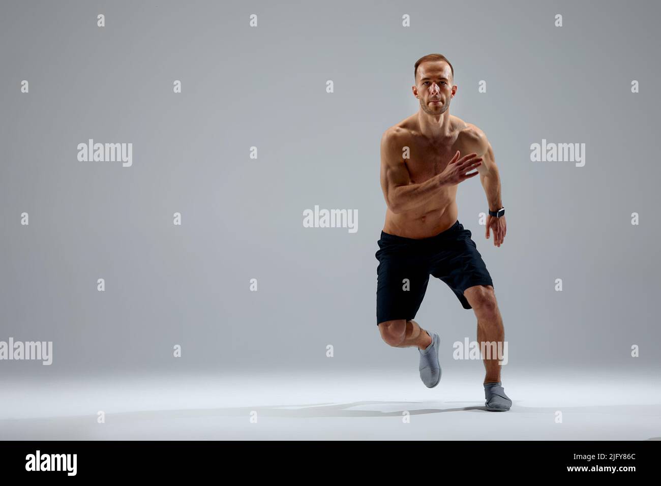 Developing endurance. Male athlete in motion isolated over gray studio ...