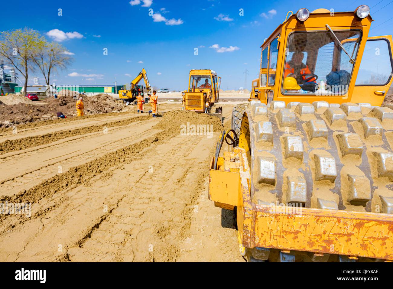 Road roller with spikes and bulldozer are compacting, leveling sand for ...