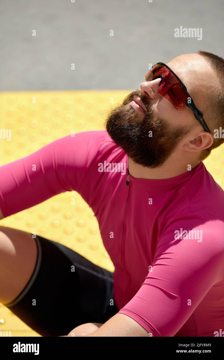 Portrait of a smiling fitness man resting while sitting on a ground at ...