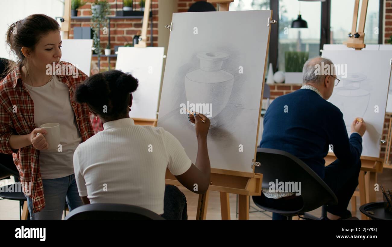 Teacher explaining to young woman how to draw vase model on canvas in ...