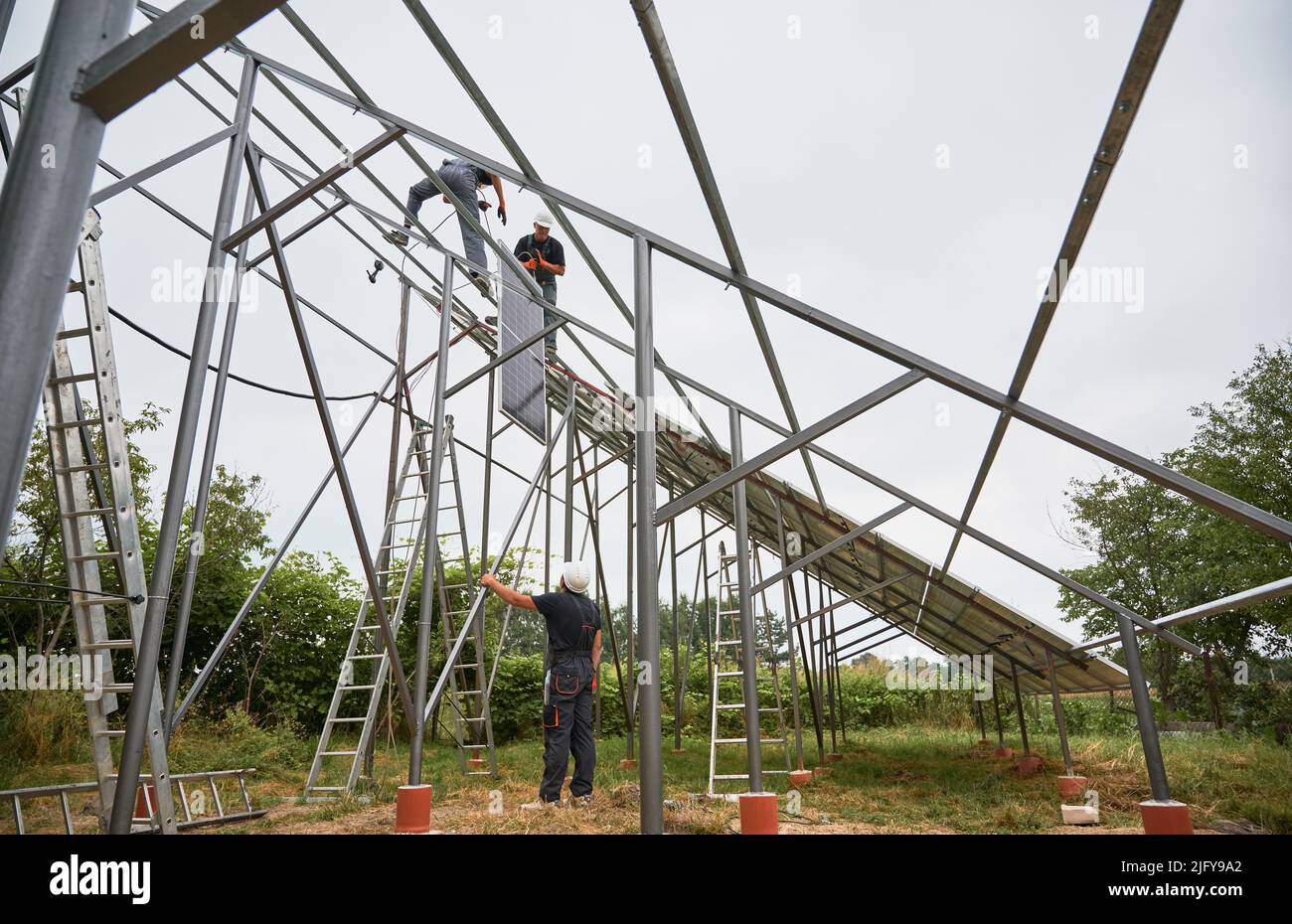 Male solar technicians standing on metal rails and lifting solar module ...