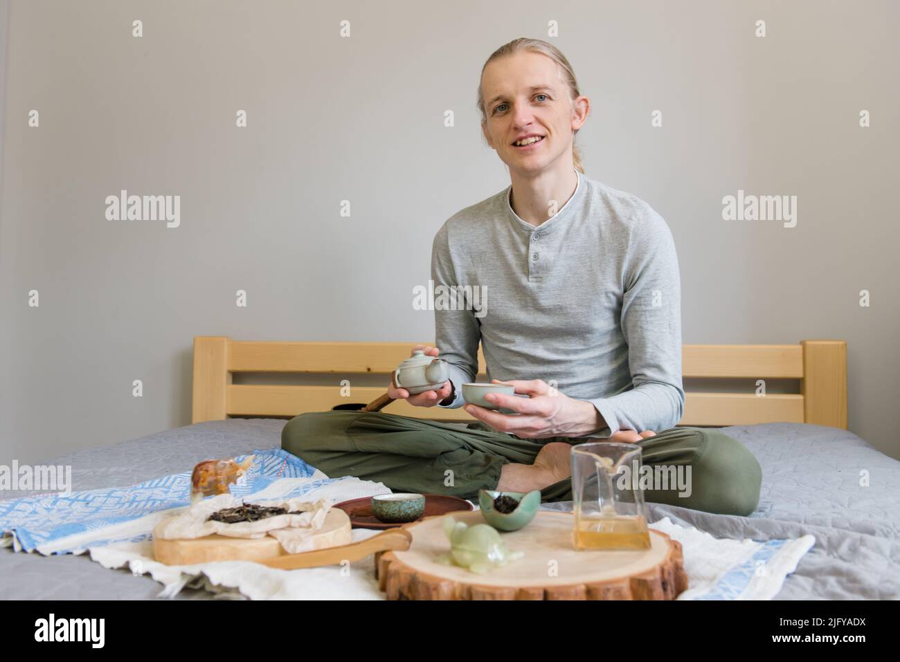 Happy man sitting on the bed, doing tea ceremony alone, stay home and ...