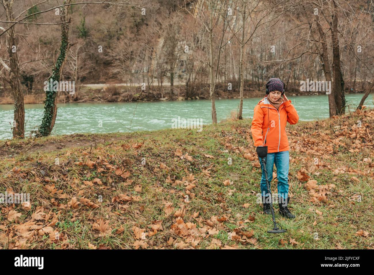 Search With A Metal Detector. A young woman in an orange jacket is ...