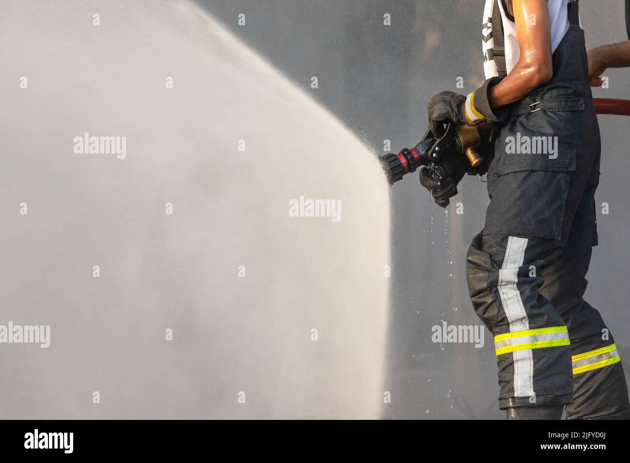 Fireman or firefighter spraying water from big water hose to prevent ...