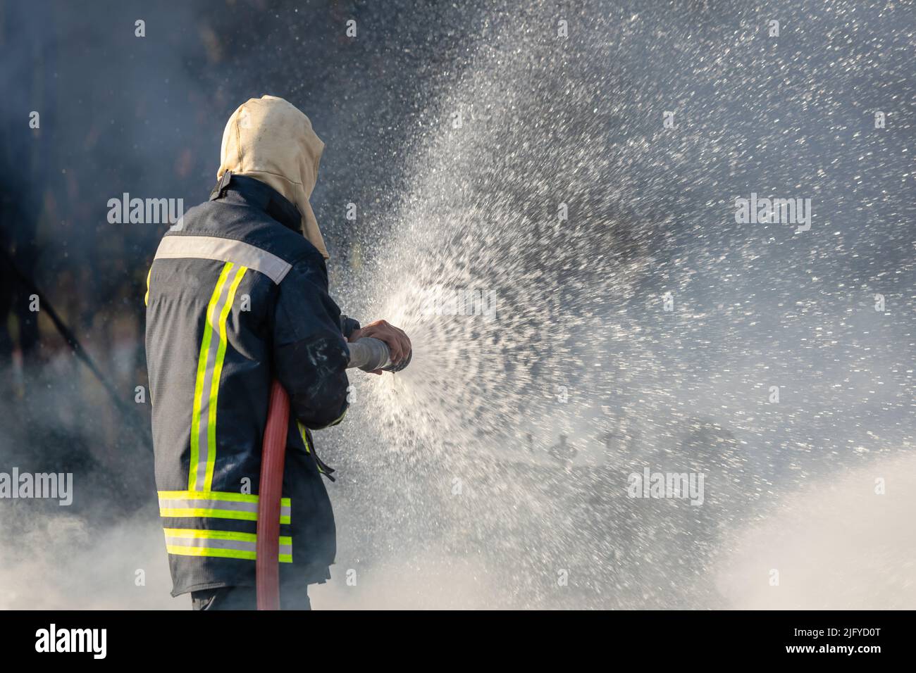 Fireman or firefighter spraying water from big water hose to prevent ...