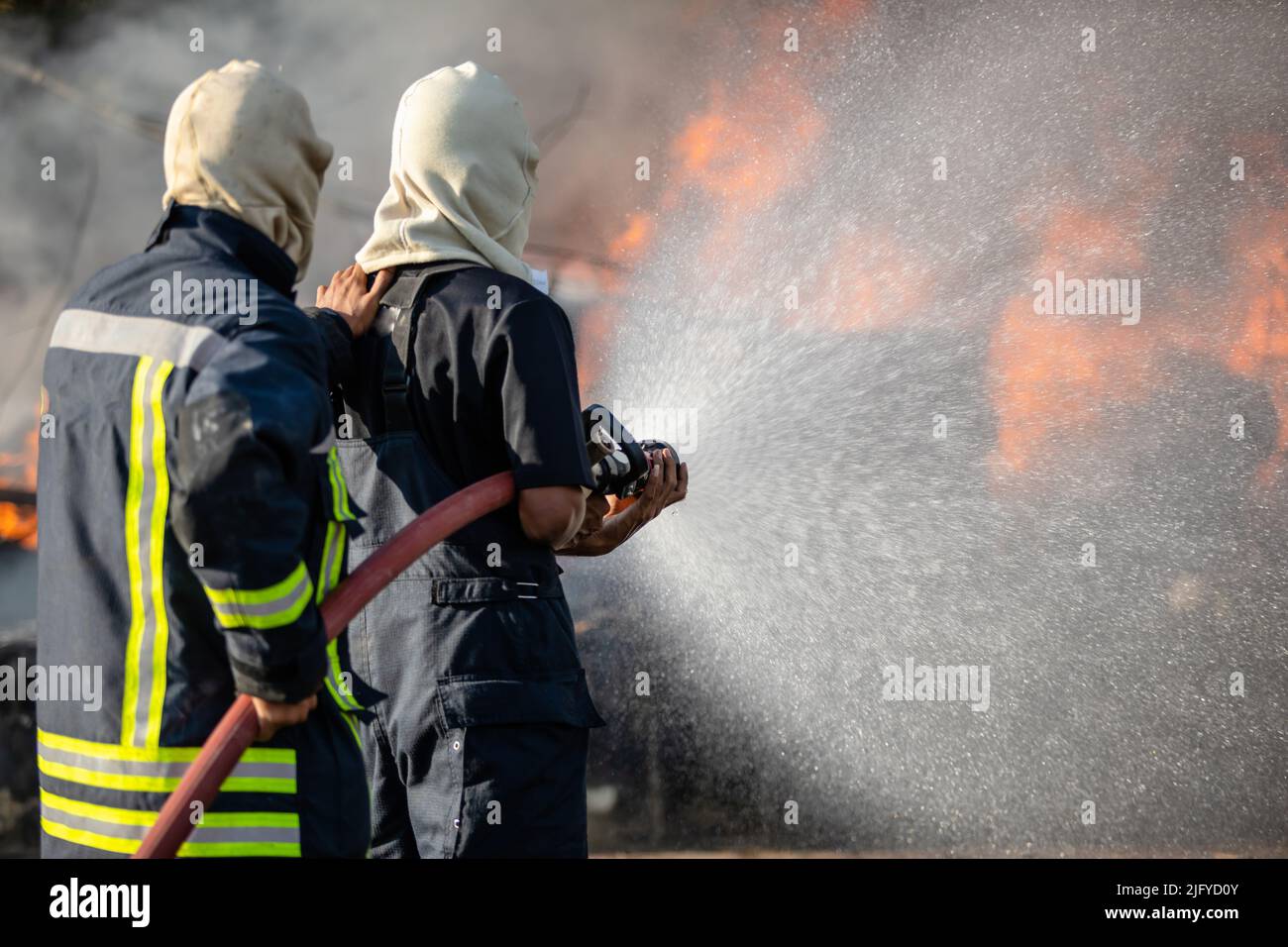 Fireman or firefighter spraying water from big water hose to prevent ...