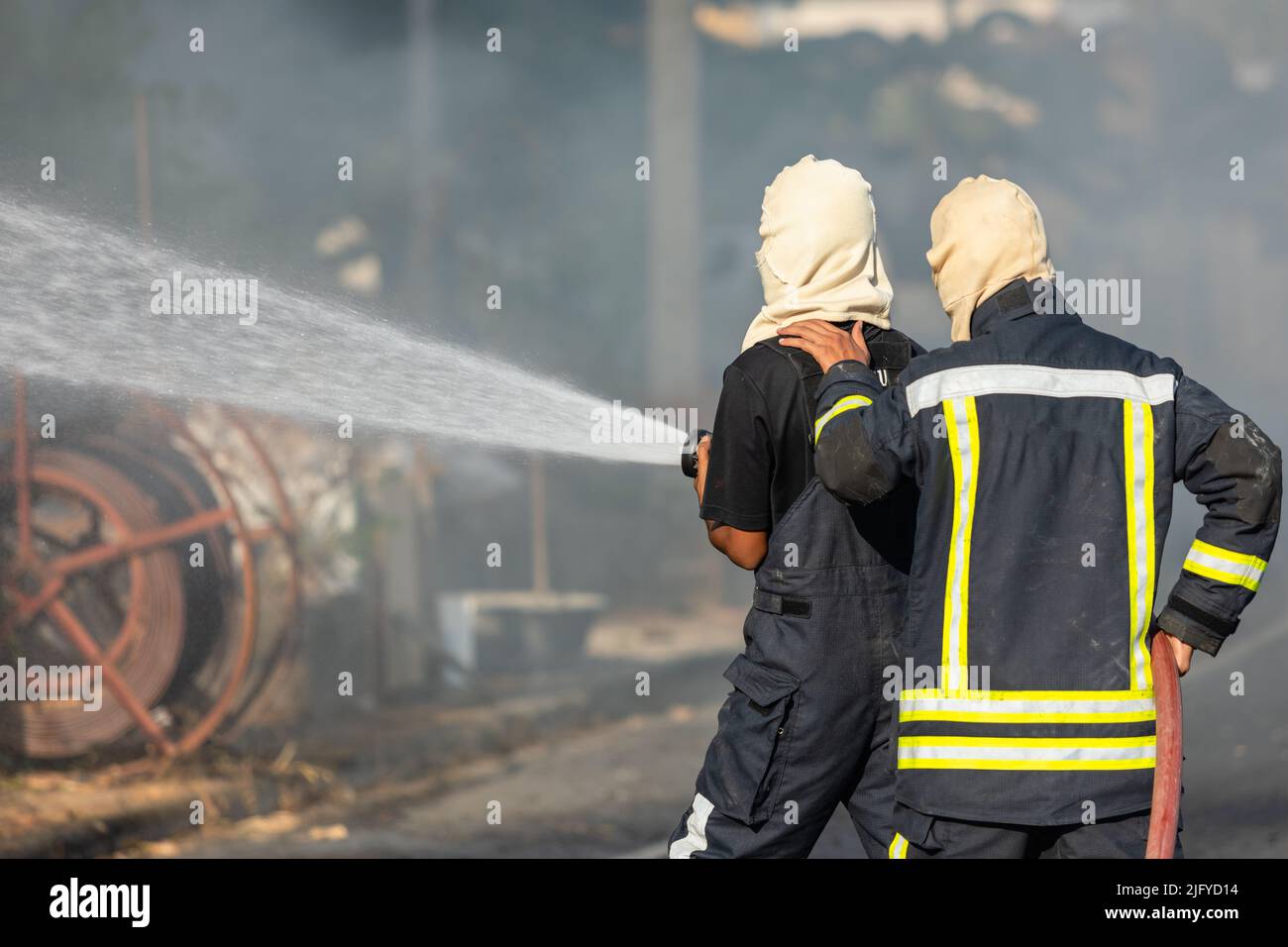 Fireman or firefighter spraying water from big water hose to prevent ...