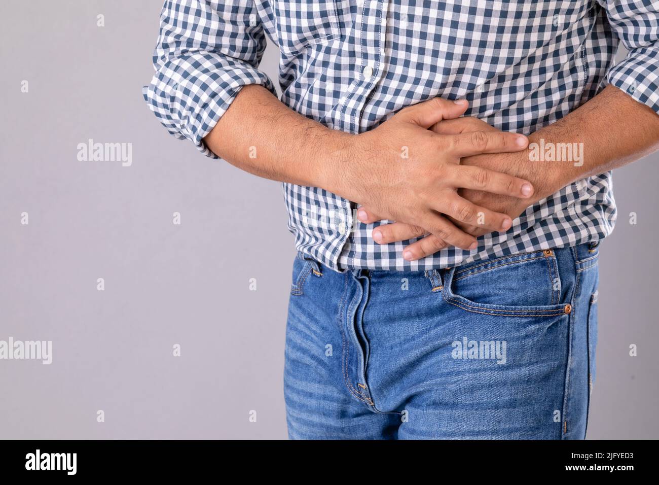 Stomach ache or pain on belly concept : Man using his hand and pressing on stomach on grey ...