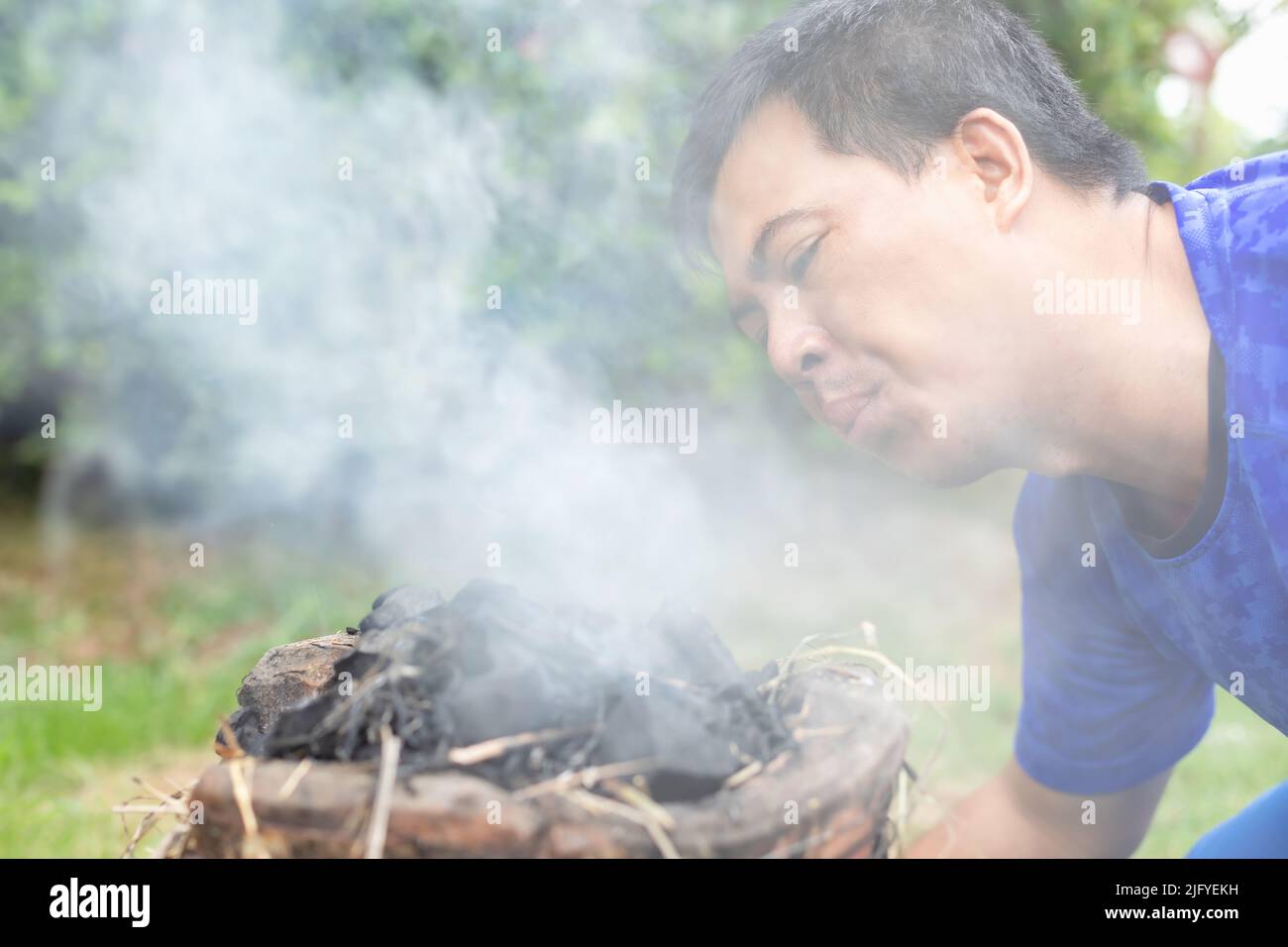 Man blowing to the stove for setting fire for cooking at outdoor. Smoke ...